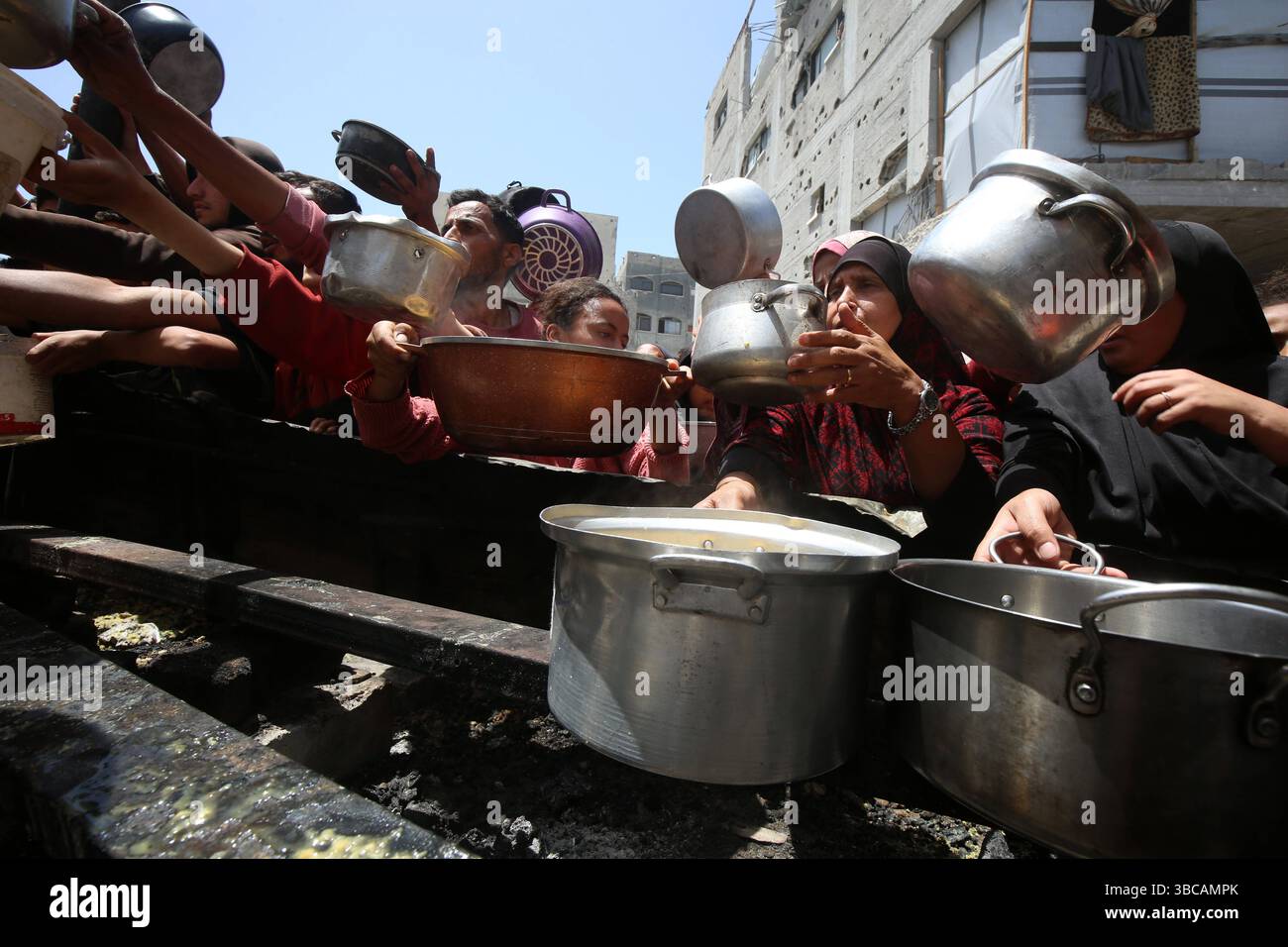 Palestinians wait in long queues to receive pots of food distributed by ...