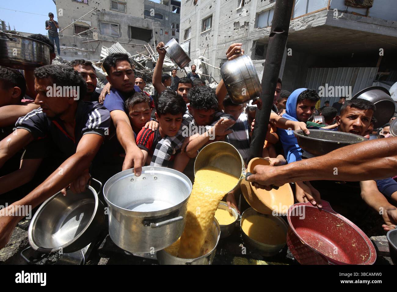 Palestinians wait in long queues to receive pots of food distributed by ...