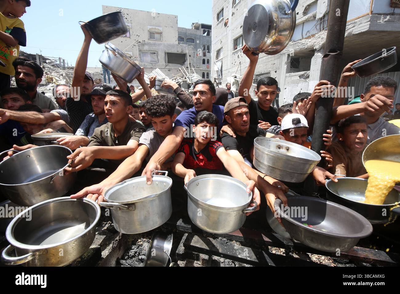 Palestinians wait in long queues to receive pots of food distributed by ...