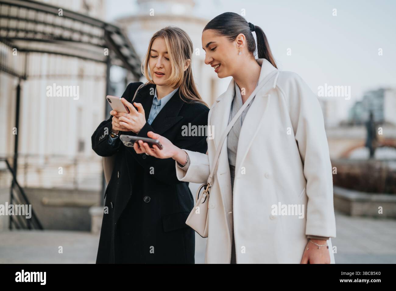Two professional coworkers discussing work together while using mobile ...