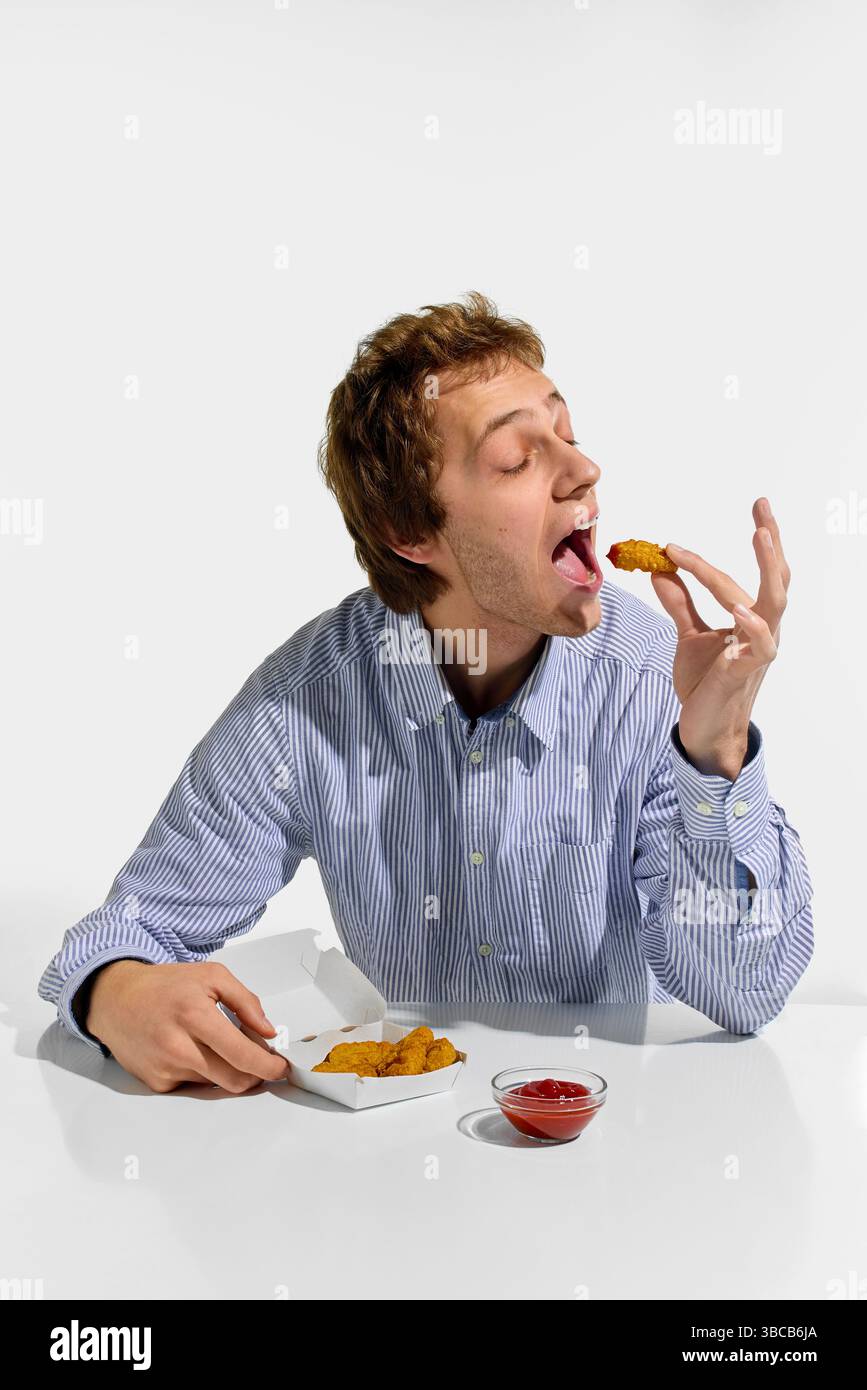 Young man about to eat crispy chicken nugget with wide open mouth and ...