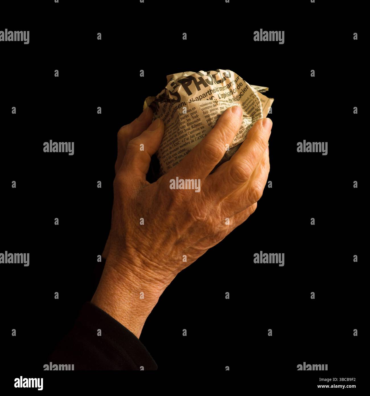 A hand gently grasps a crumpled newspaper, symbolizing the weight of ...
