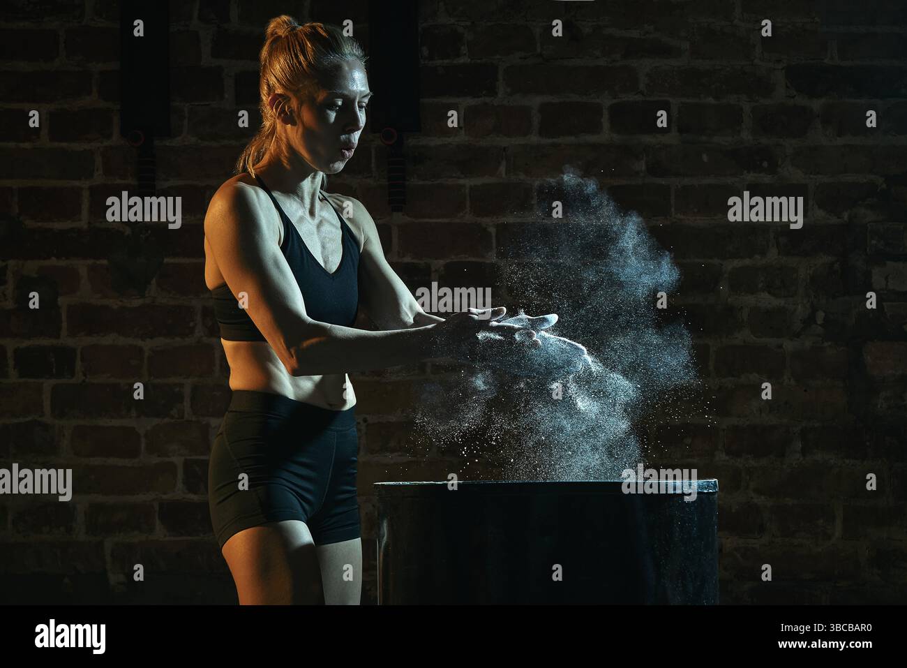 Focused female athlete prepares for lift by clapping chalked hands ...