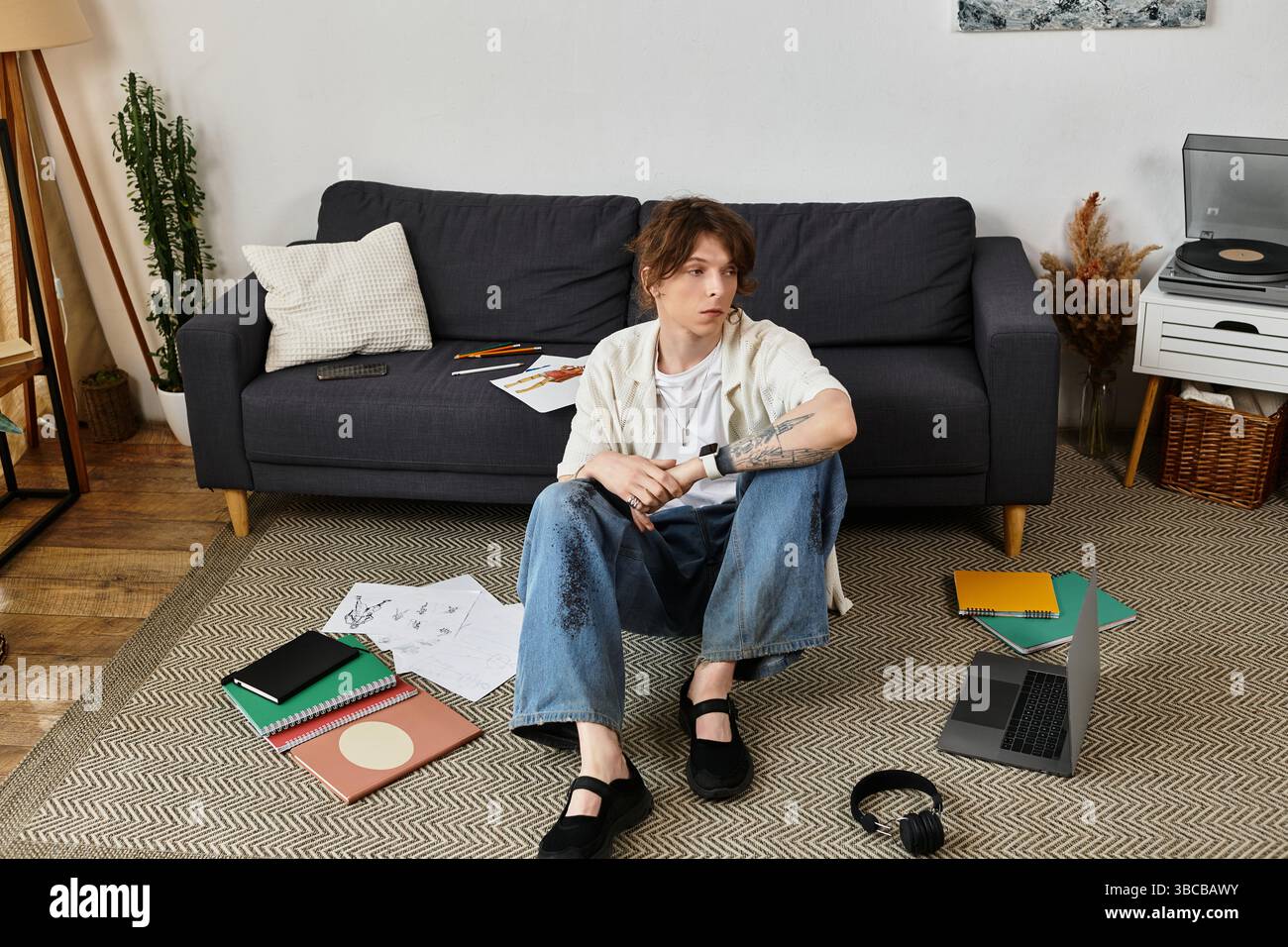 A young student sits comfortably on the floor with study materials and ...