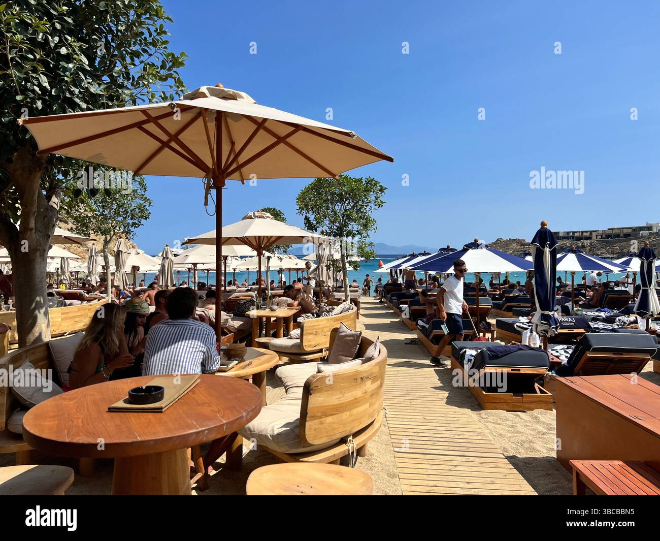 Guests relax under parasols at a stylish beach club on the coast of ...