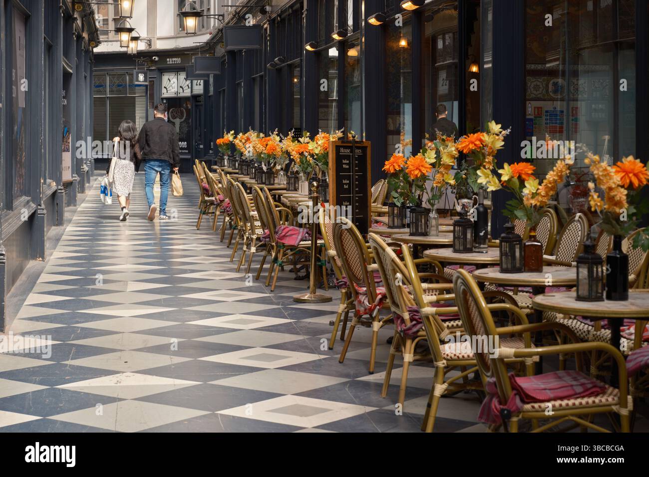 Café tables with floral displays line the tiled walkway of Castle ...