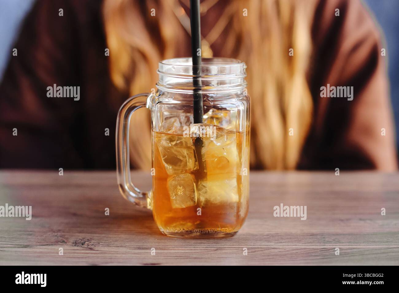 Glass of iced tea. Transparent jar with straw. Cold refreshing drink on table. Ice cubes in ...