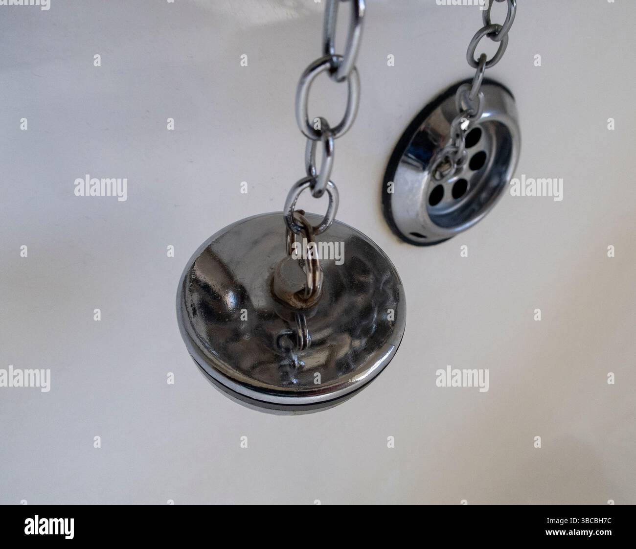 Old fashioned chrome bath plug hanging by it's chain in a white enamel ...