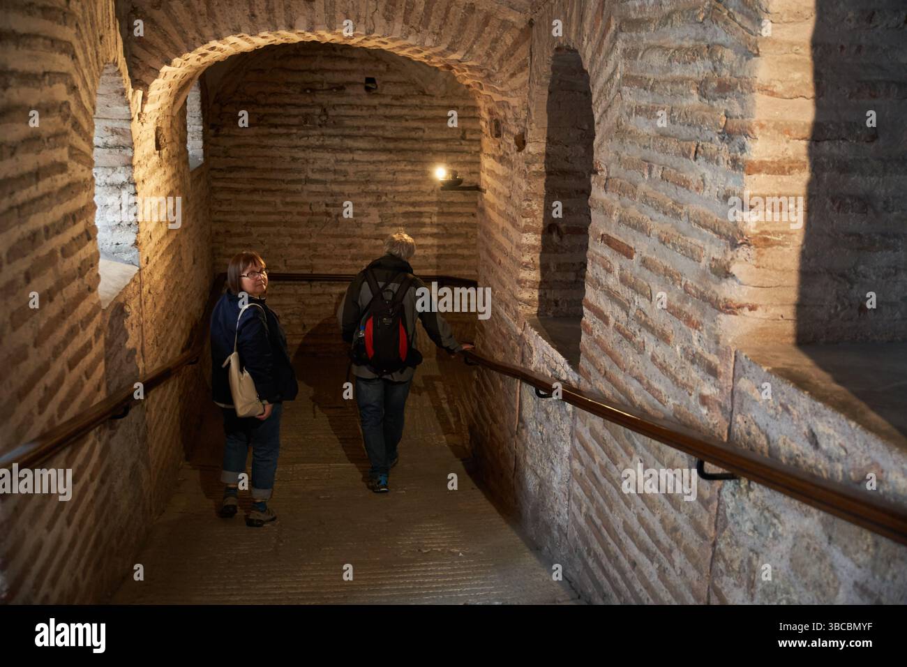 Tourists explore an ancient arched stone ramp in the dimly lit historic ...