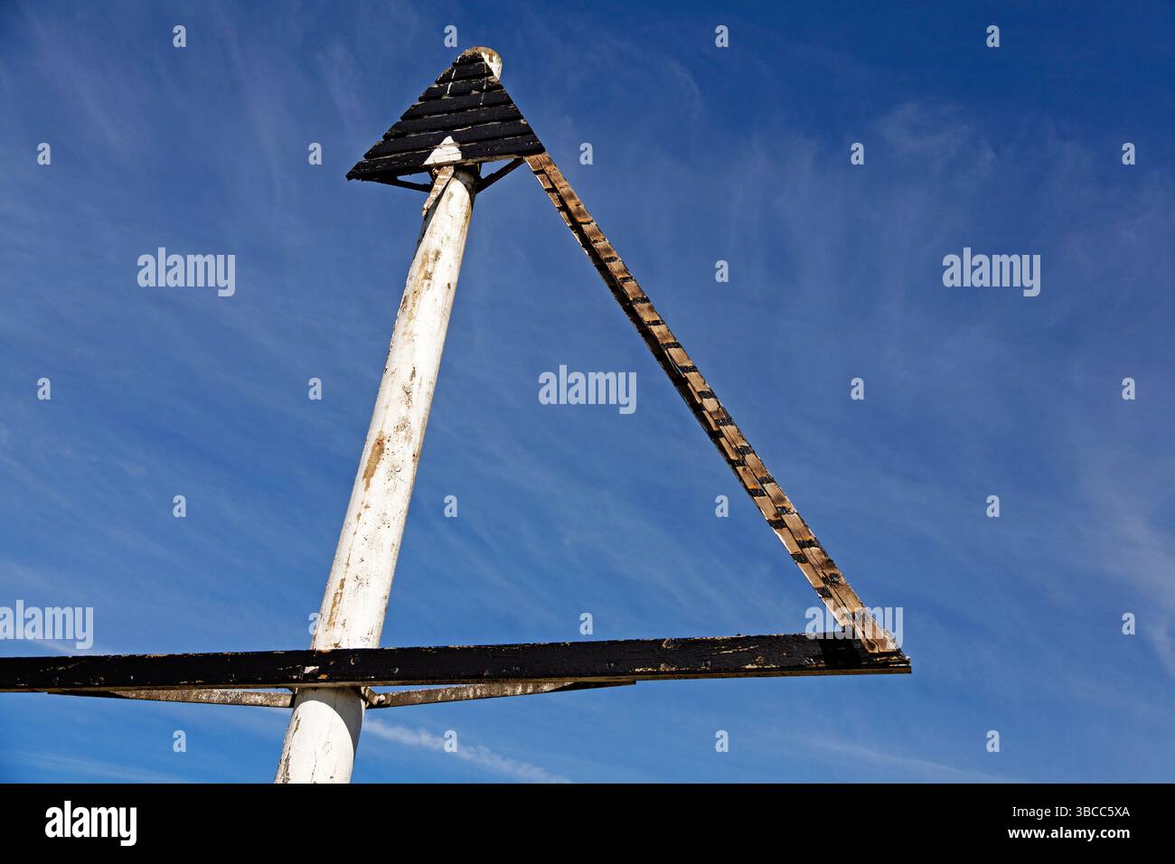 A damaged triangular nautical marker mounted on a weathered white pole ...