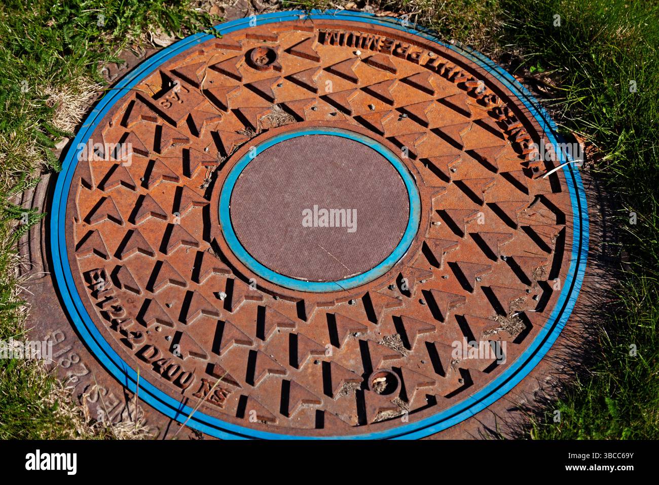 A circular rusty brown manhole cover with a textured pattern and blue ...