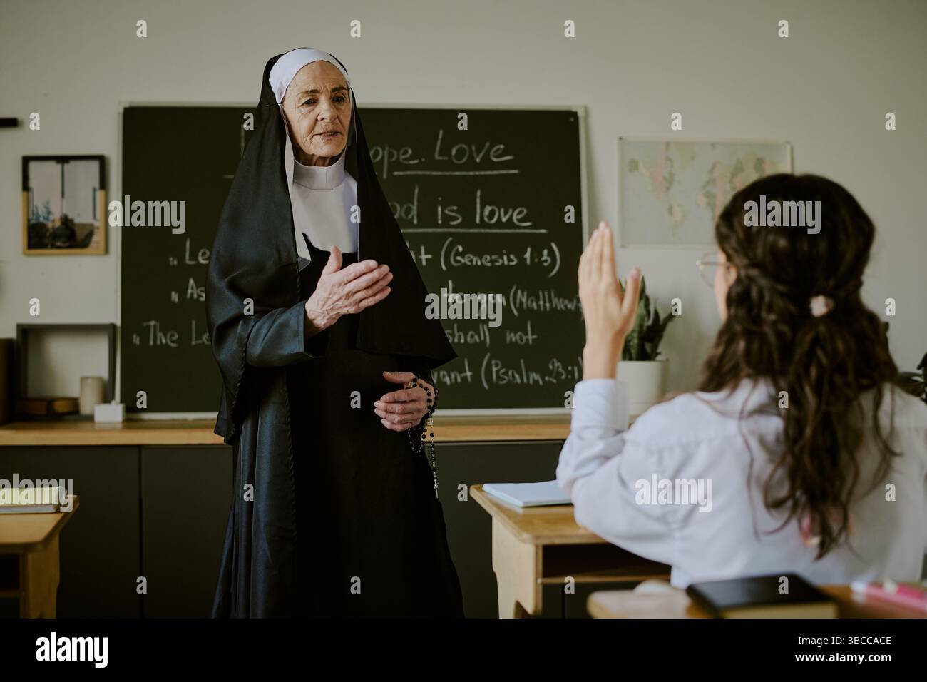 Elderly nun standing in classroom teaching while student seated at desk ...