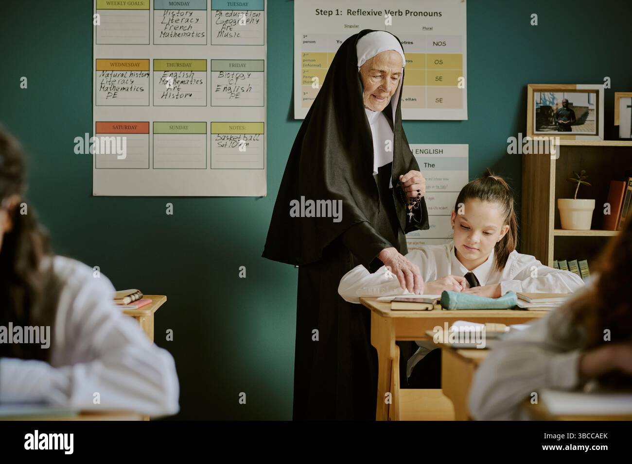 Elderly nun assisting young student with their schoolwork in classroom ...