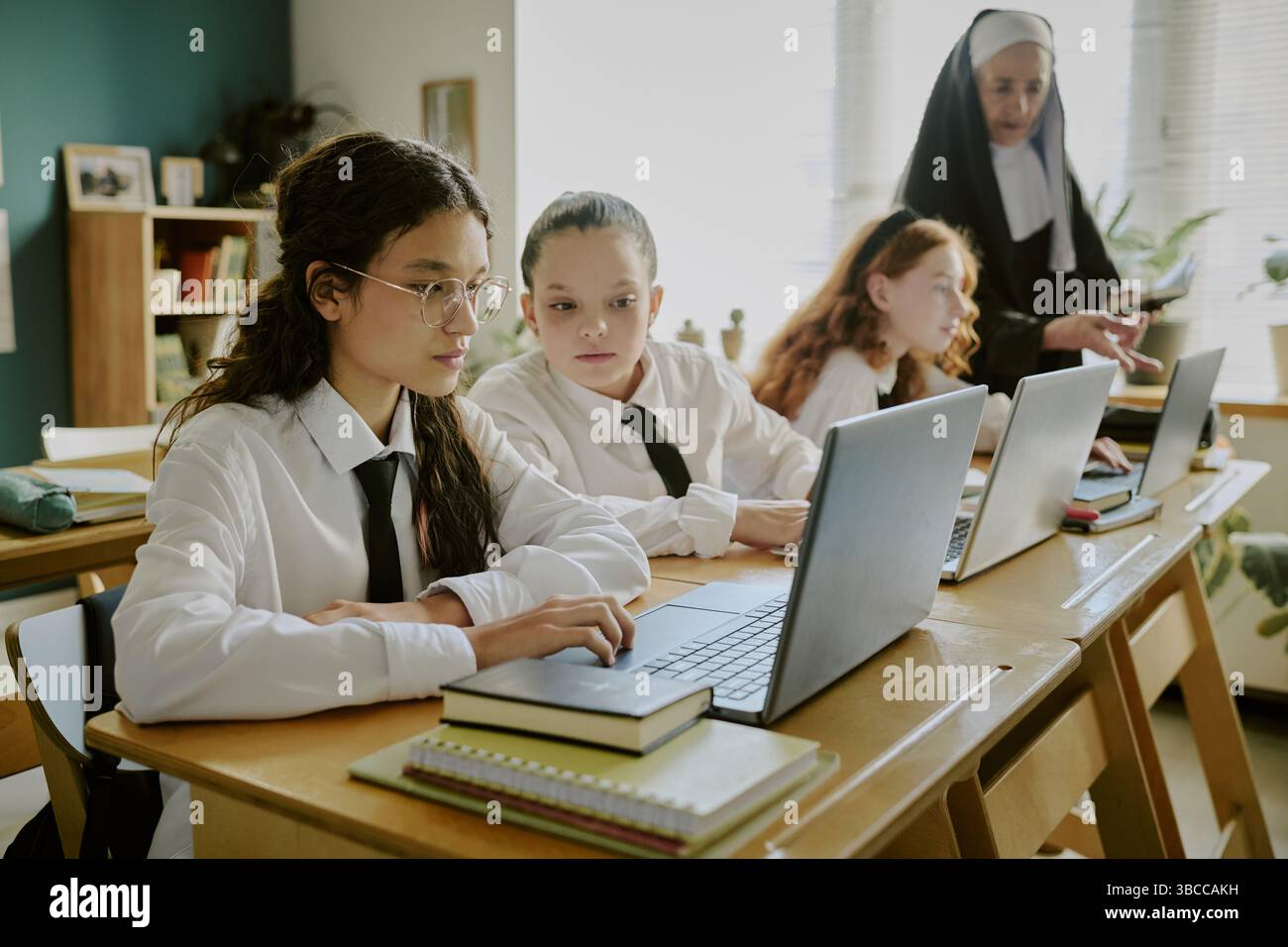 Group of students wearing uniforms sitting at desks and working on ...