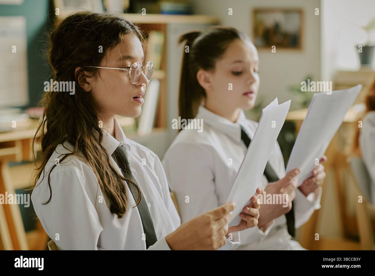 Two girls wearing school uniforms reading documents in classroom ...