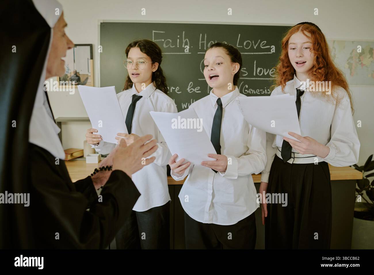 Group of students in uniform practicing singing while facing teacher in ...