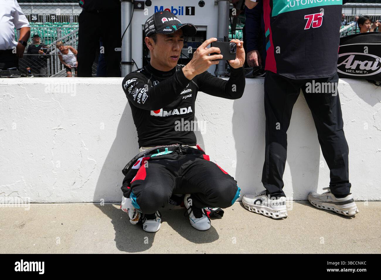Takuma Sato, of Japan, photographs a car as it leaves the pit area ...
