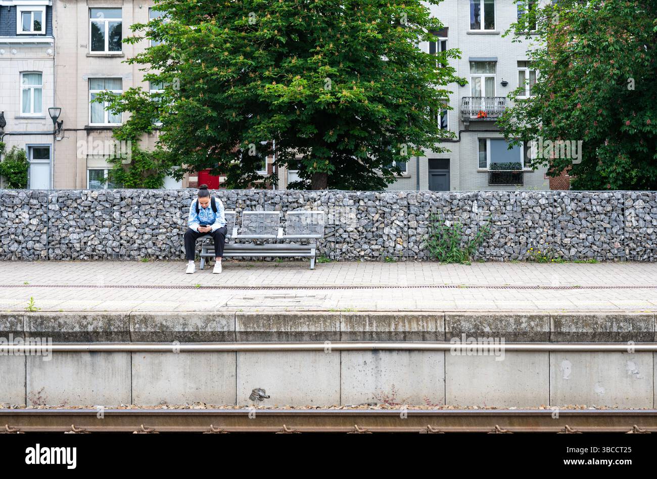 Young woman sitting on a bench at the railway station of Jette ...