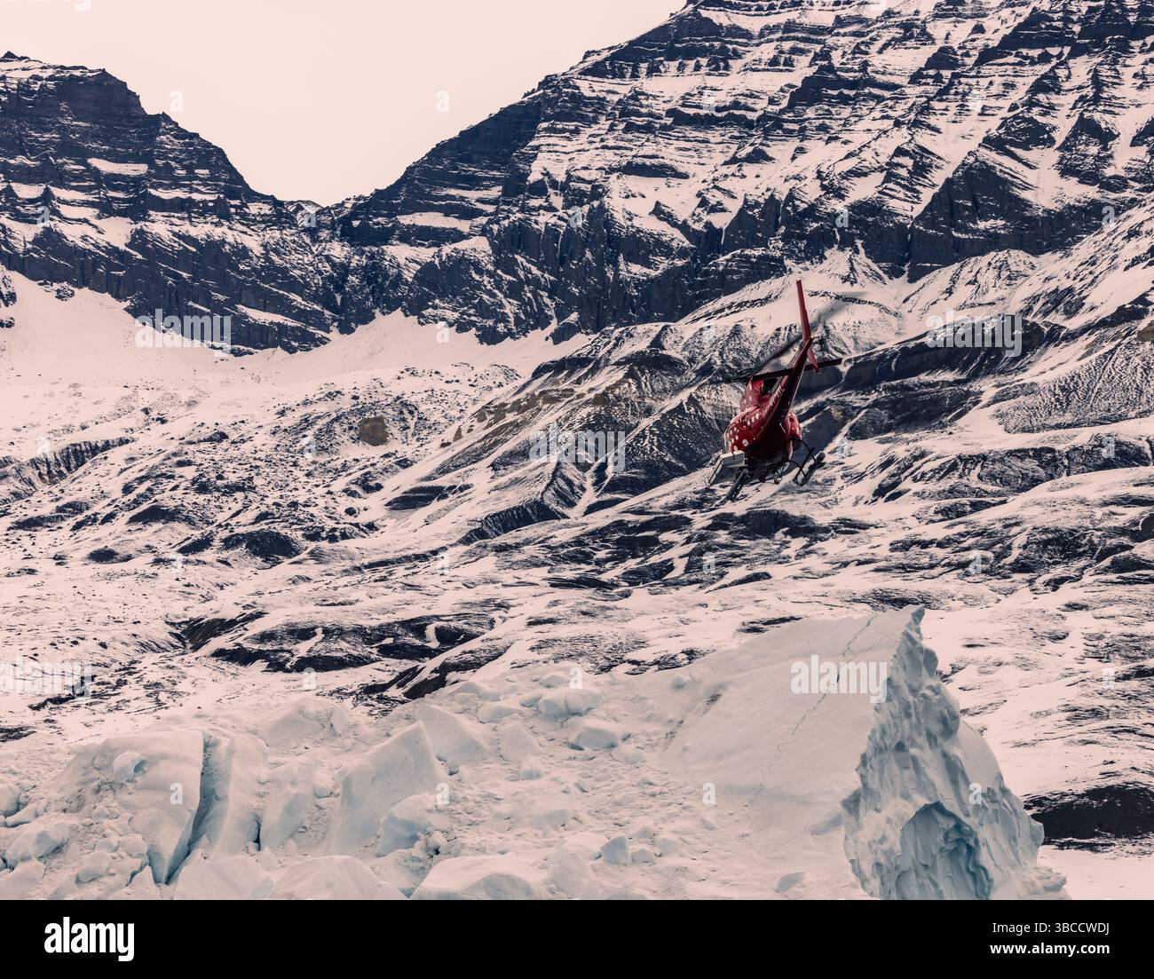 Red helicopter flying low above icy terrain and jagged peaks in West ...
