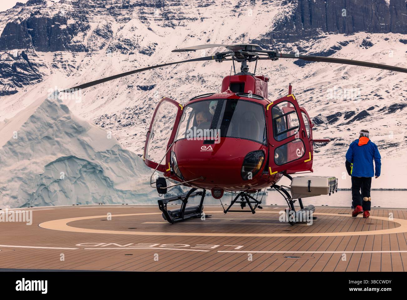Red helicopter on helideck beside iceberg and snowy mountains in East ...