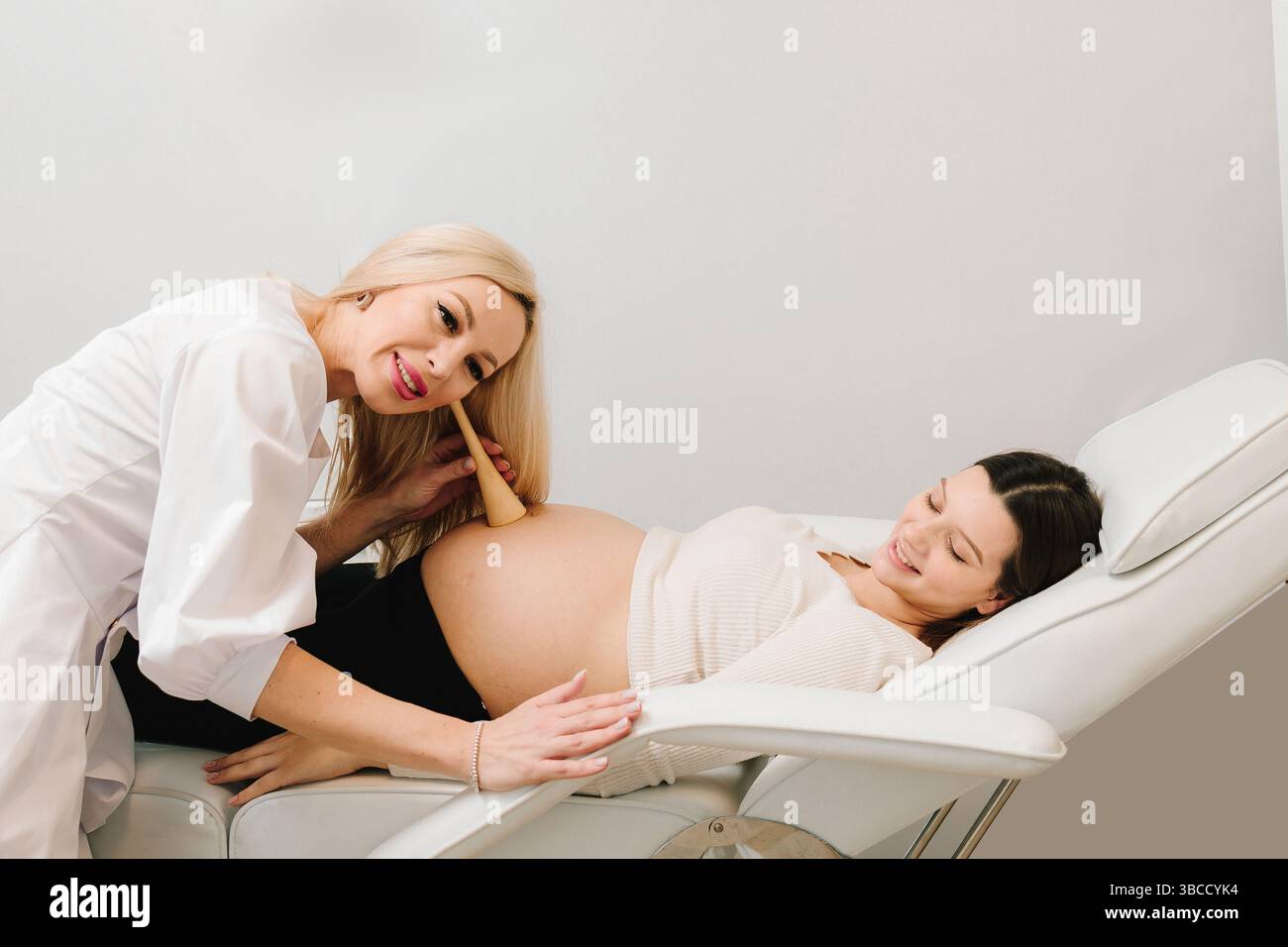 Gynecologist leans a fetal stethoscope to a pregnant woman's belly and ...