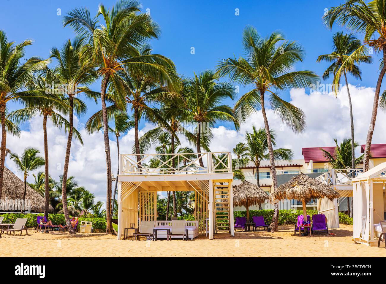 White beach cabana with palm trees and sun loungers under blue sky at ...