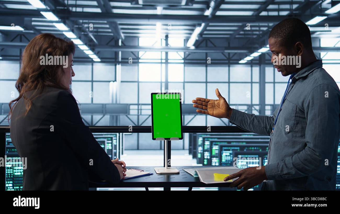 Programmers in data center brainstorming, using mockup tablet, observing equipment analytics ...