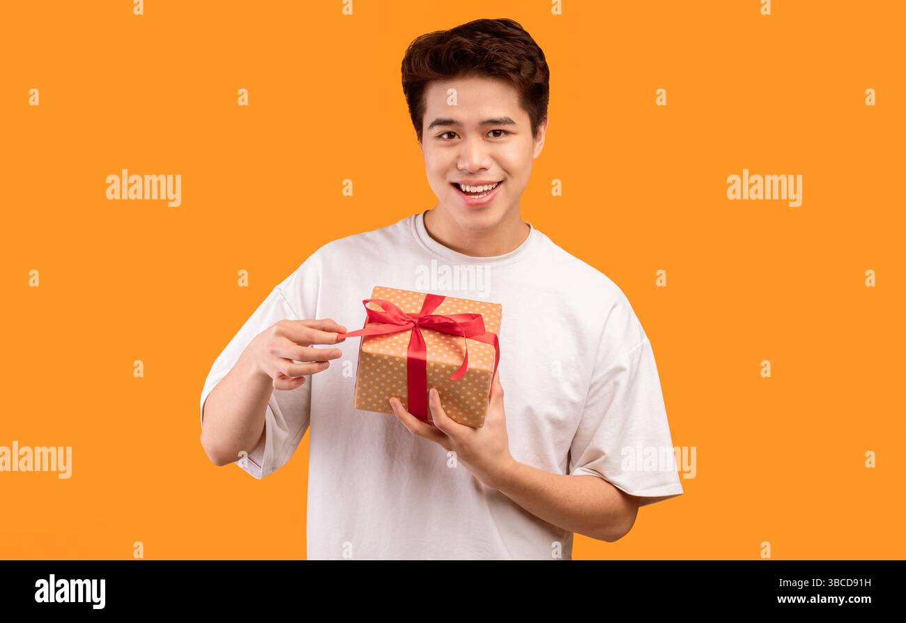 Happy asian guy holding present box pulling ribbon Stock Photo - Alamy