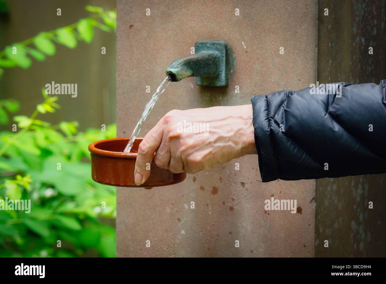 close-up of a hand filling a shallow ceramic vessel from a wall ...