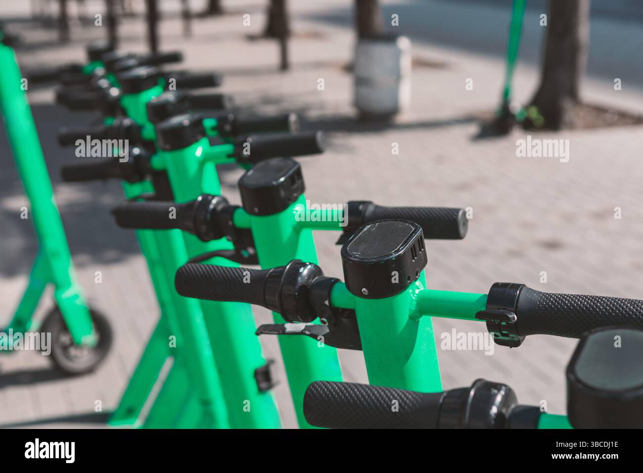 Row of green electric scooters, handlebars angled towards the viewer ...