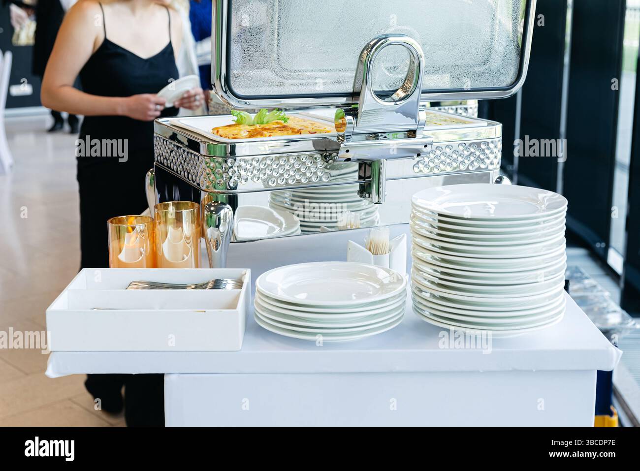Stack of clean white plates beside a chafing dish filled with food at ...