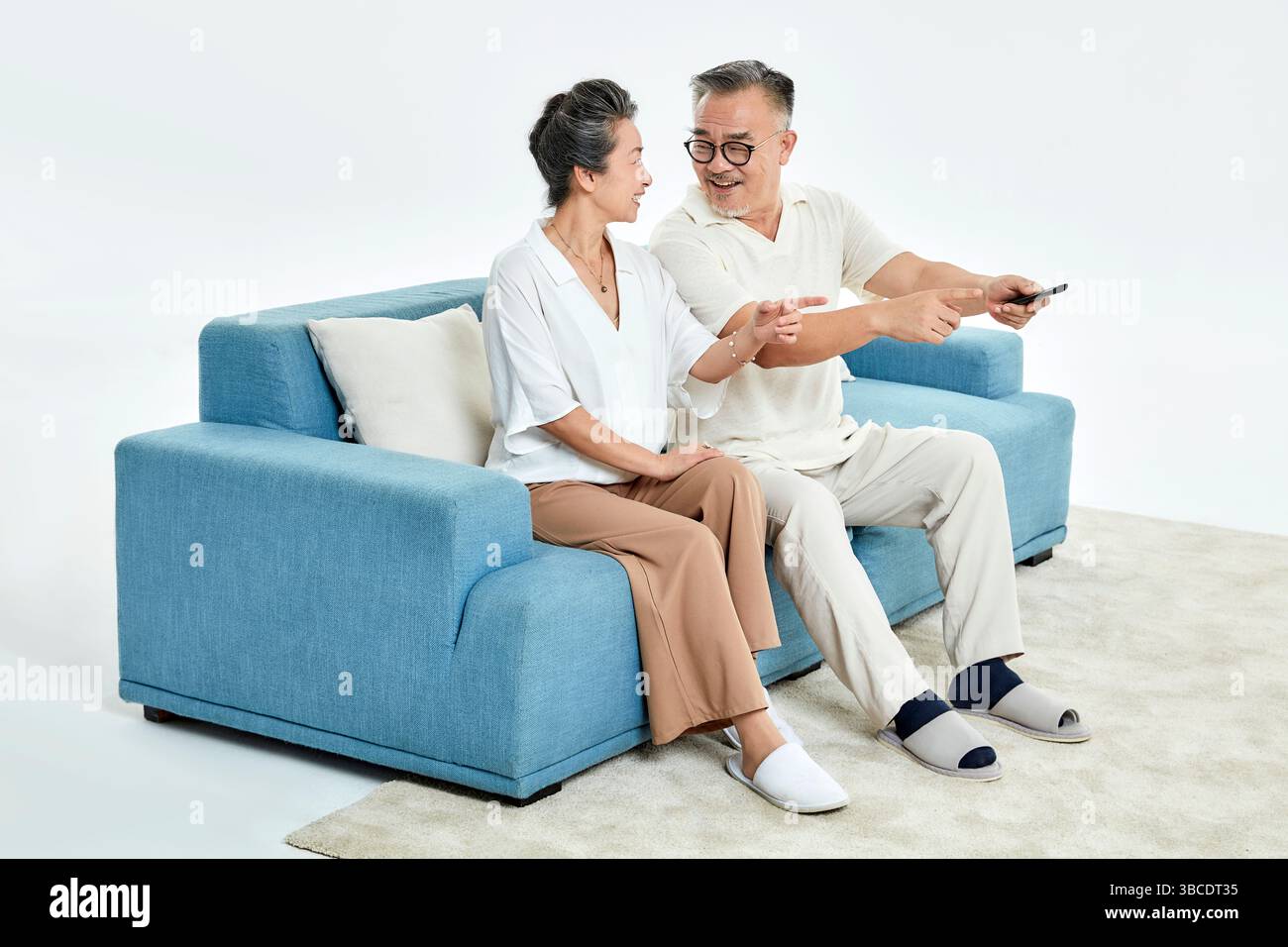 An elderly couple sitting on the sofa watching TV with a remote control ...