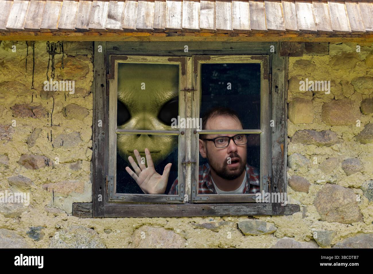 Scared man looking out of the window of an old farm with an alien ...