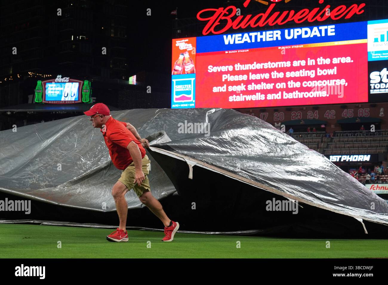 A member of the Busch Stadium grounds crew helps cover the field during ...