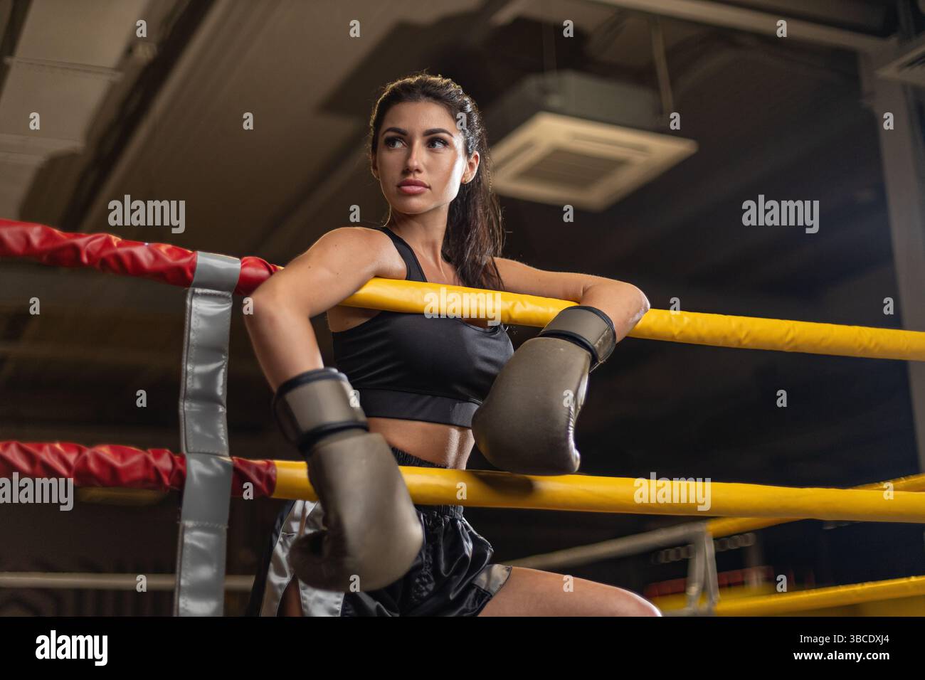young female boxer leans against the ropes in a gym wearing boxing ...