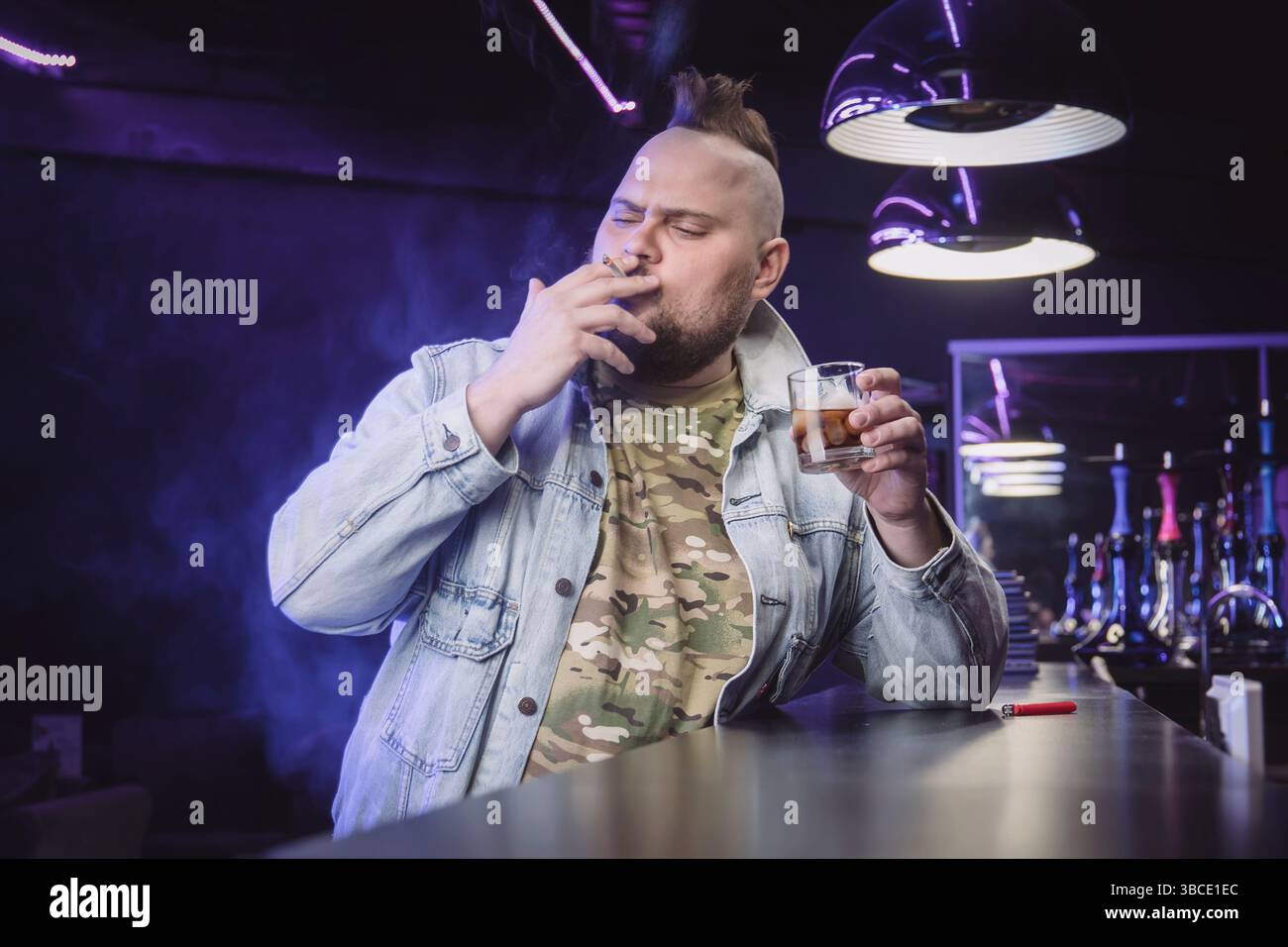 an informal young man with a mohawk on his head smokes and drinks ...