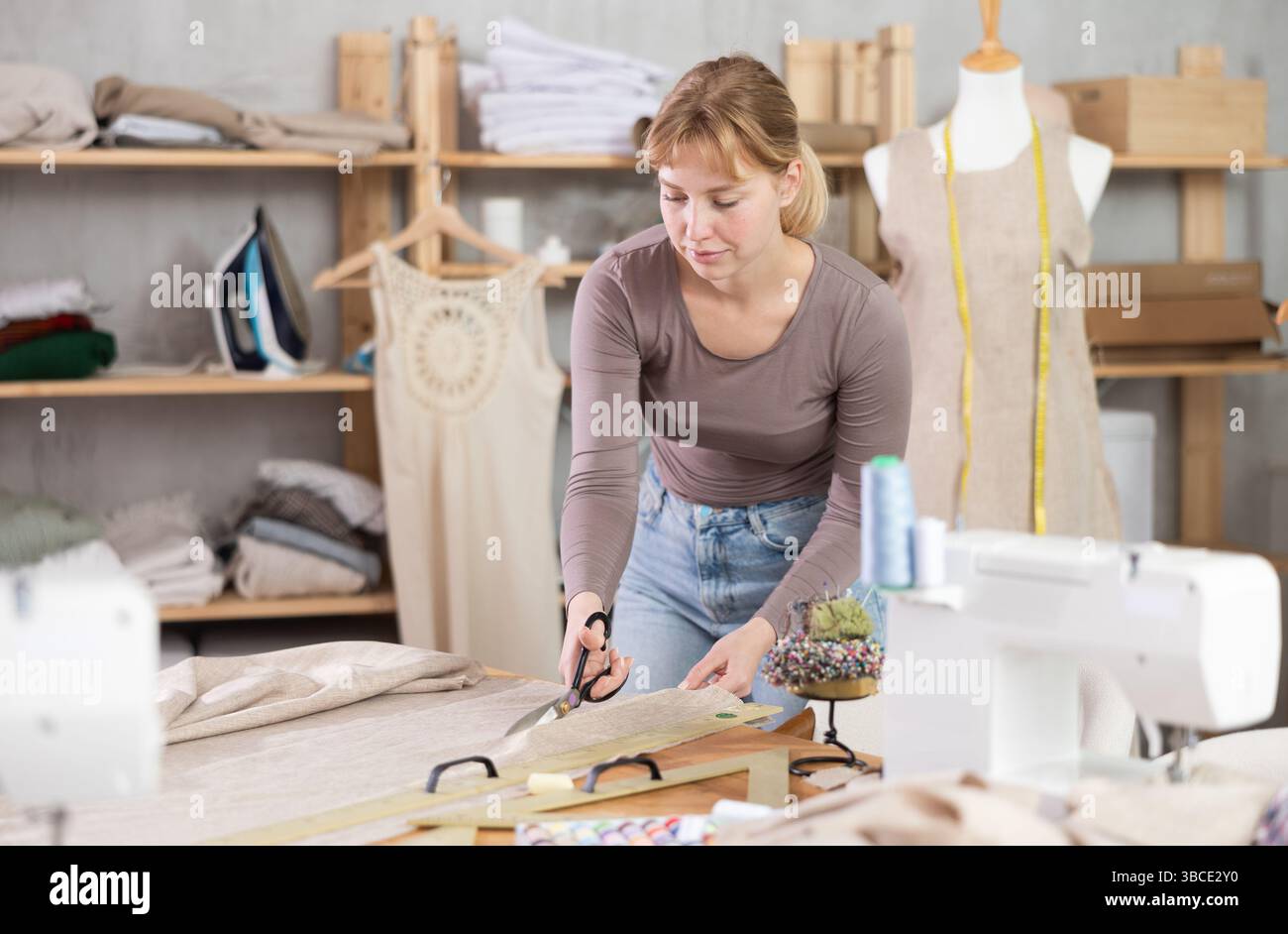 Female dressmaker using fabric shears to cut linen in workshop Stock ...