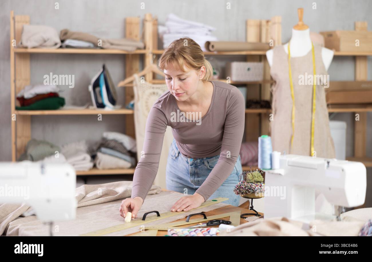 Female seamstress marking pattern lines on piece of linen with chalk ...