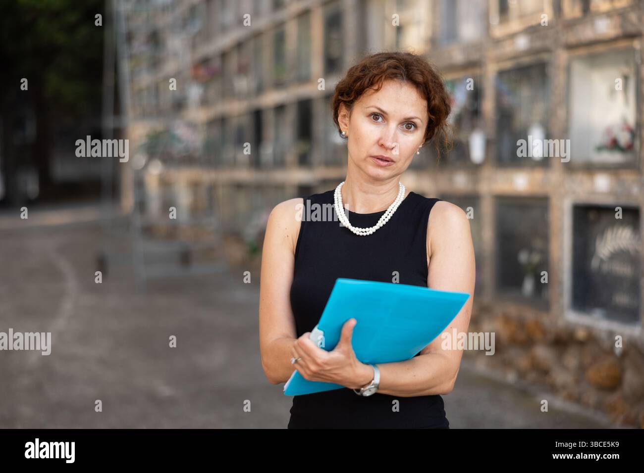 Female cemetery employee in black dress stands with report and writes ...