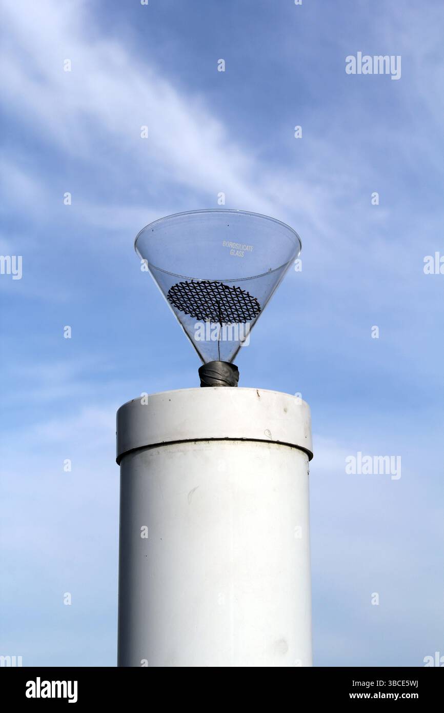 Weather rain gauge on a white post against a blue sky with wispy clouds ...