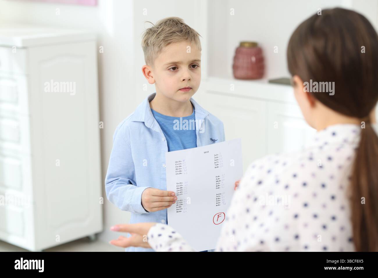 School grade. Sad boy showing answer sheet with bad mark to his mother ...