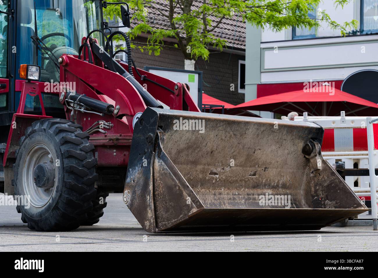 A large red loader stands parked on a city street, ready for ...