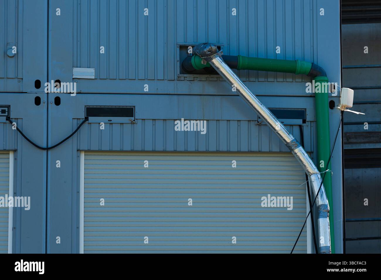 A large industrial building features a silver metallic pipe extending ...