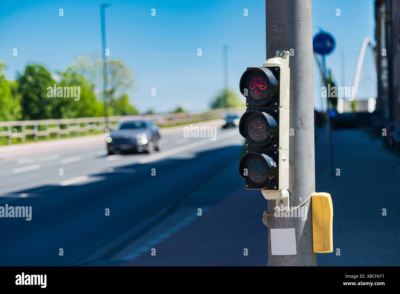 A traffic light with red signals stands beside a road where a car is ...