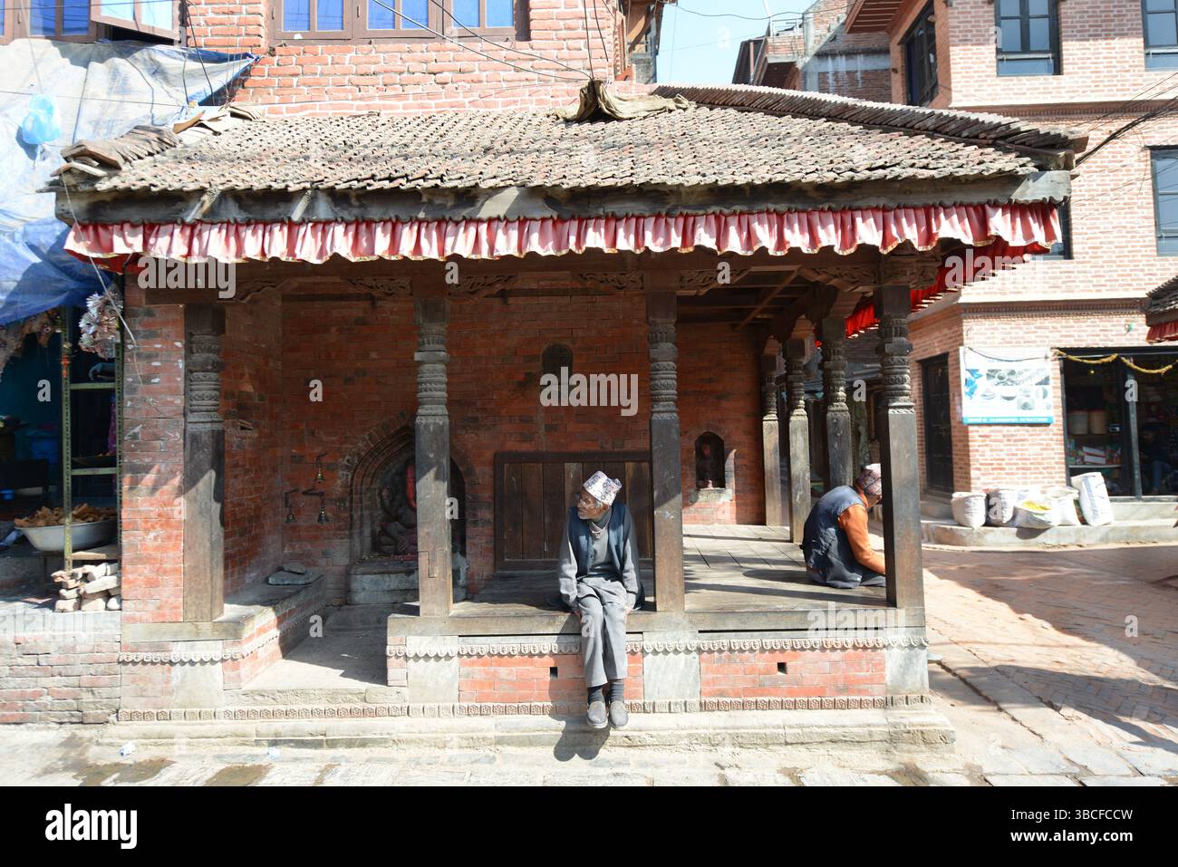 A Nepali man sitting on street level balcony of a traditional house in the old city of Bhaktapur ...