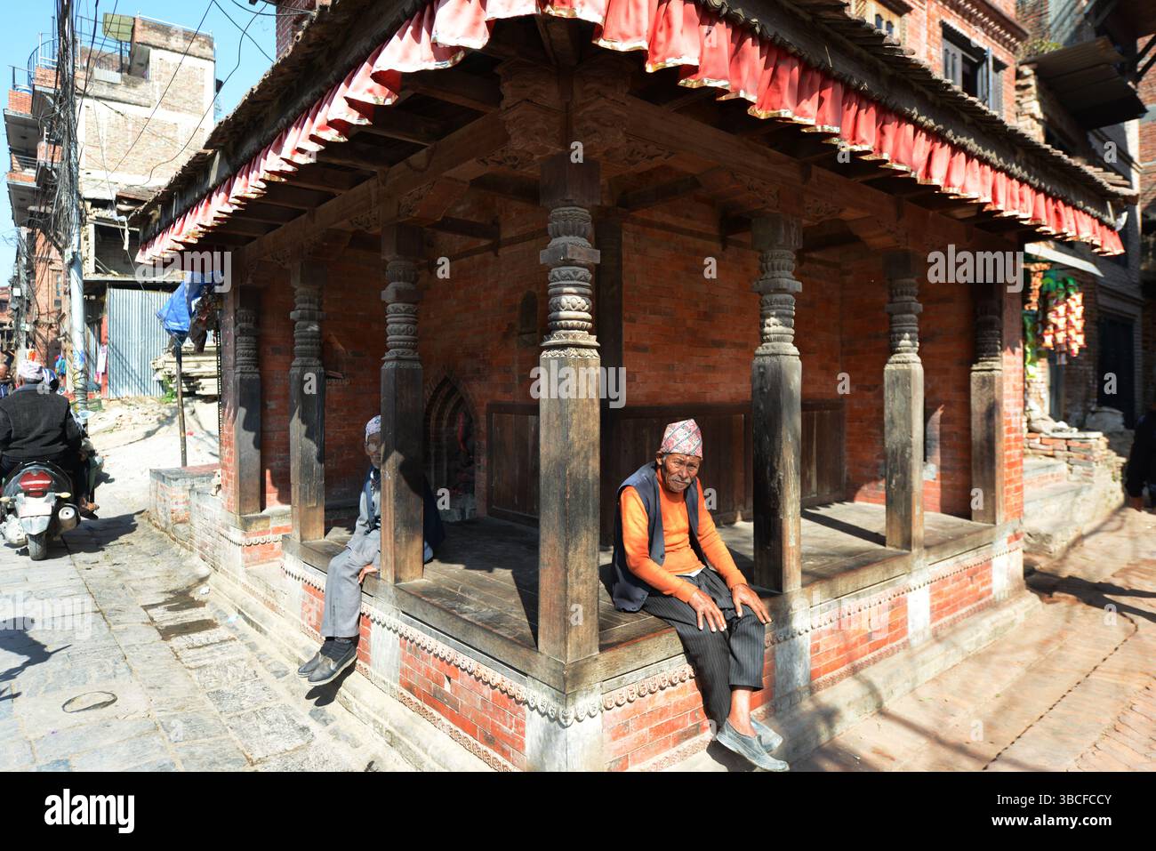 A Nepali man sitting on street level balcony of a traditional house in ...