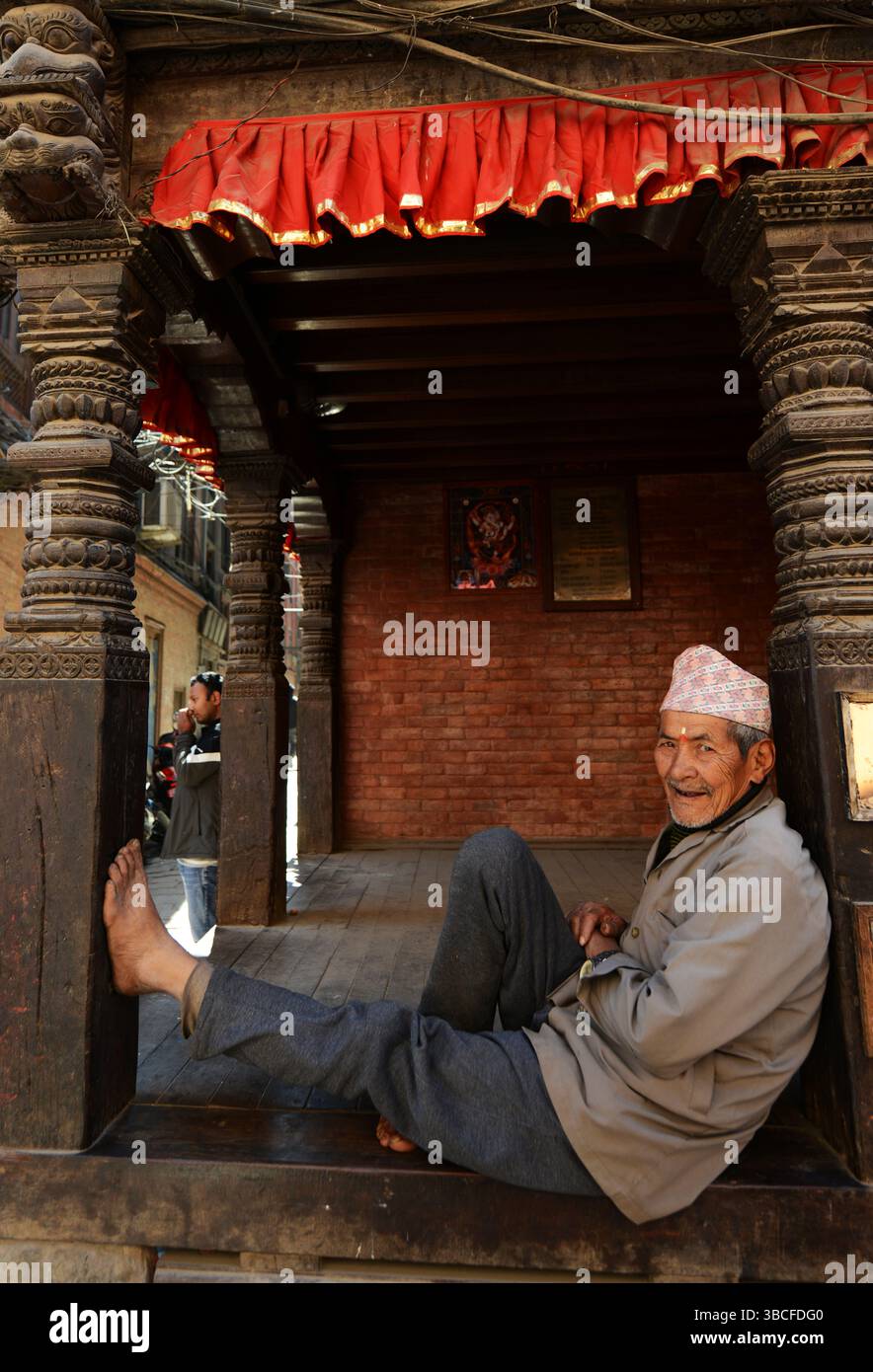 A Nepali man sitting on street level balcony of a traditional house in the old city of Bhaktapur ...