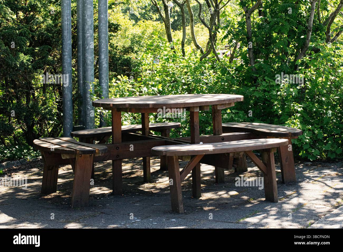 Round wooden picnic table with benches in a lush and sunny park ...