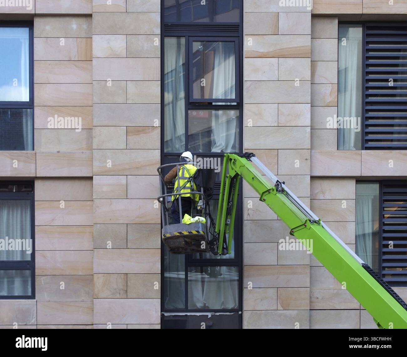 An unidentifiable construction worker in a green aerial work platform ...