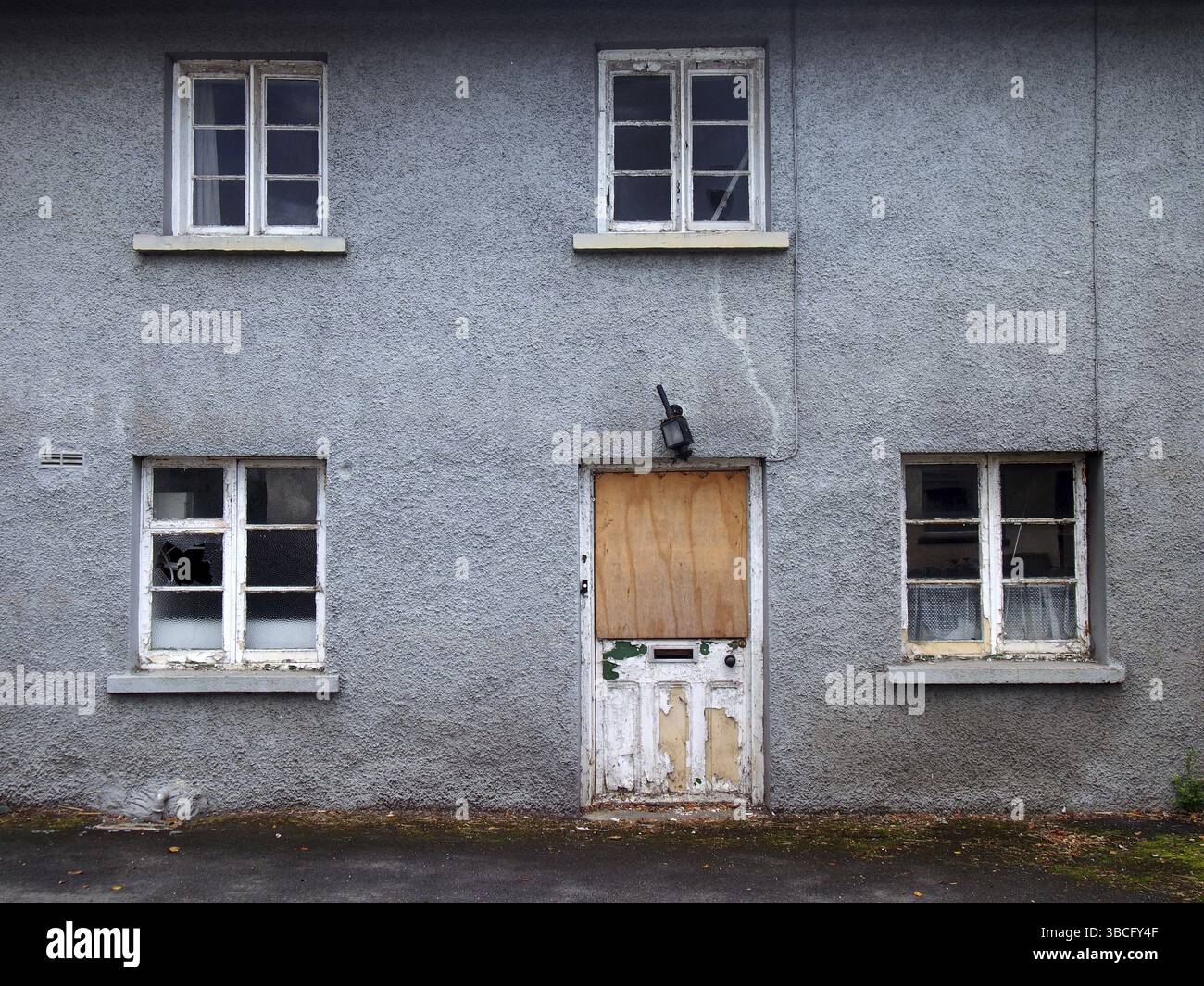 An old abandoned grey derelict house on a residential street with dirty broken windows and a ...